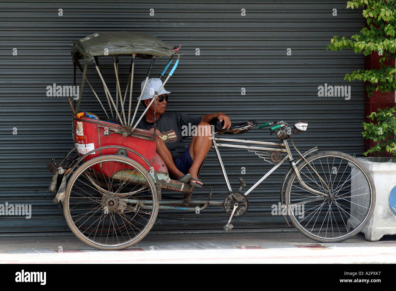 Bicycle rickshaw driver relaxing on the side of the road, Chiang Mai ...