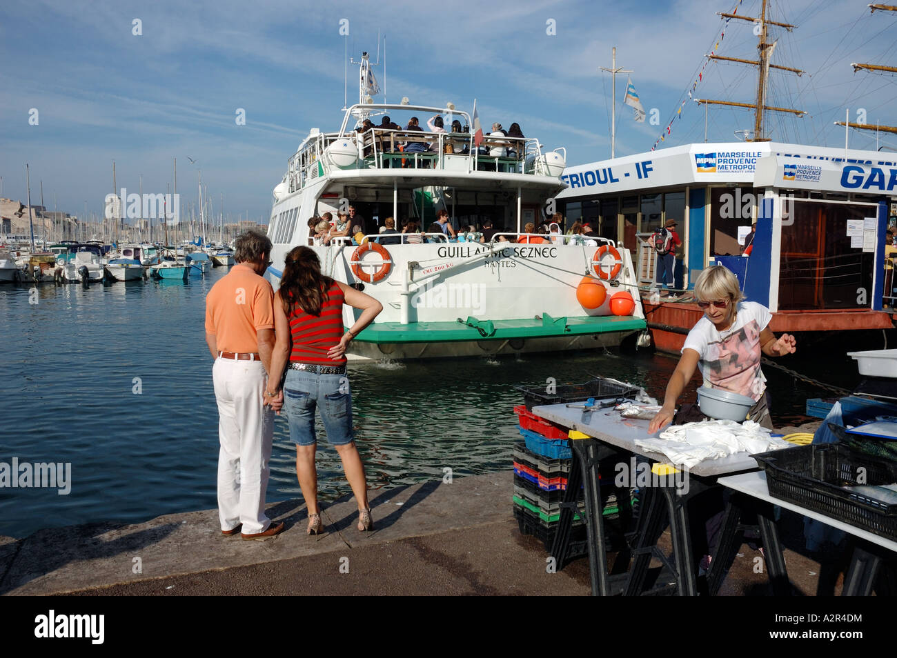 A caucasian couple looking at boat beside a french fishmonger at fish ...