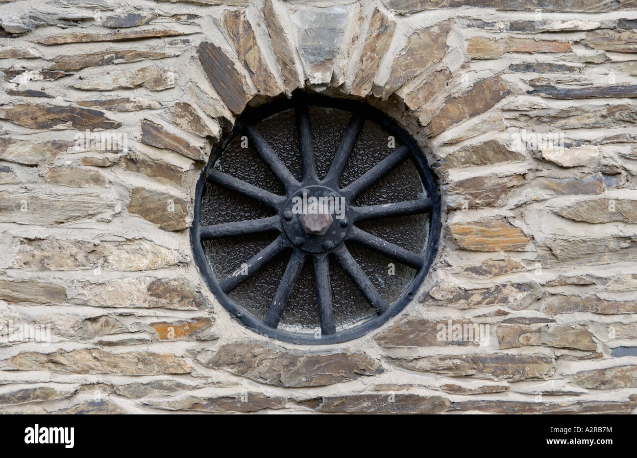 Old spoked cast-iron wheel used as rustic window detail on rural stone ...
