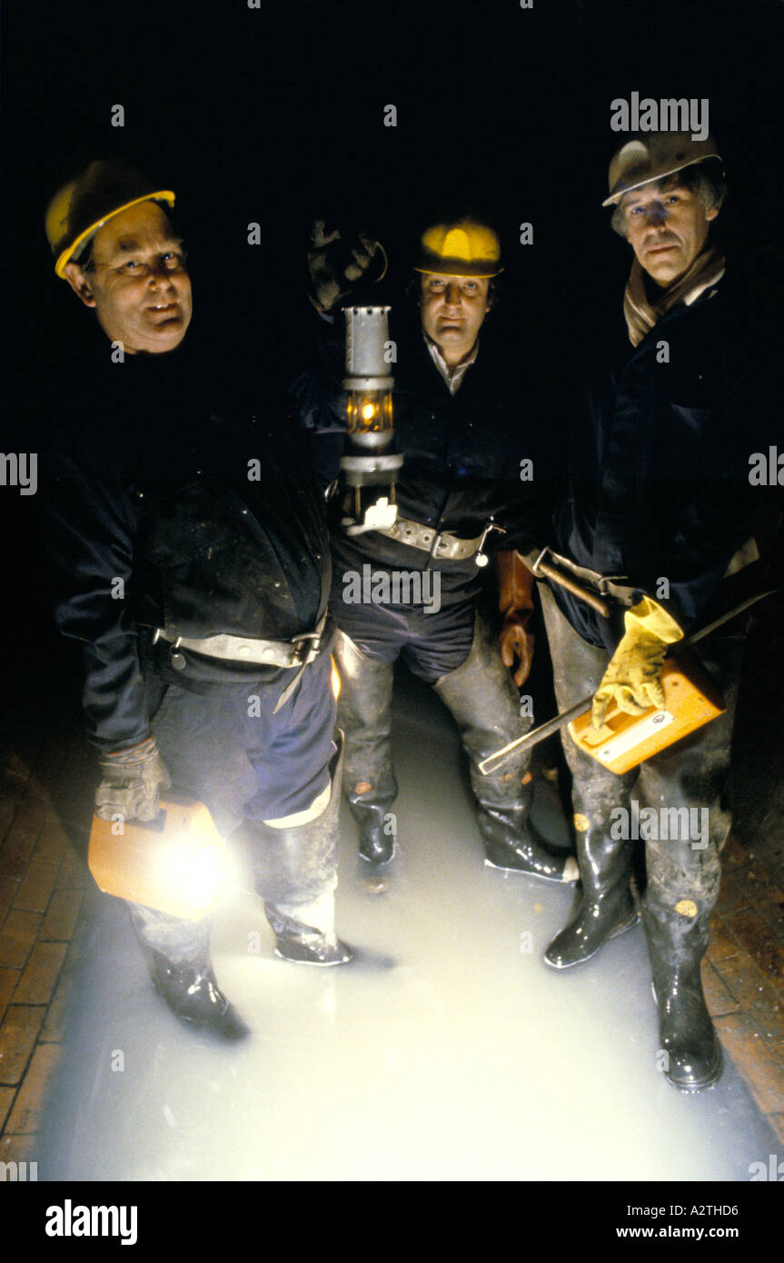 sewage workers in darkness underground holding work lantern wearing ...