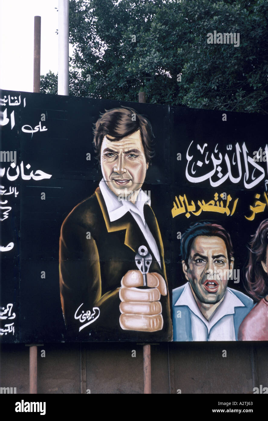 a painted billboard advert with arabic writing and man pointing a gun ...
