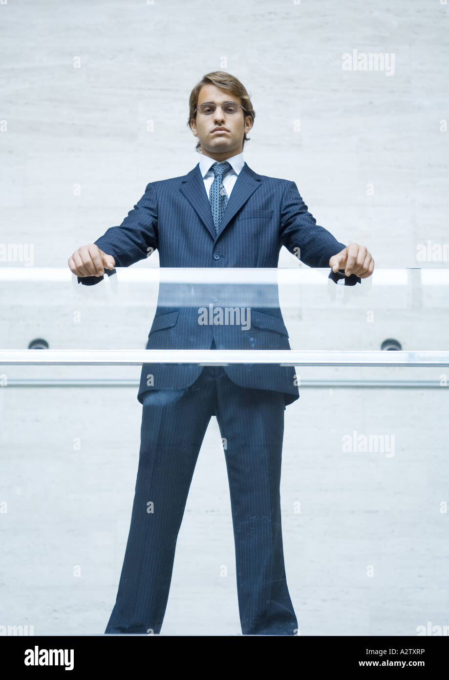 Businessman standing with hands resting on transparent guard rail ...
