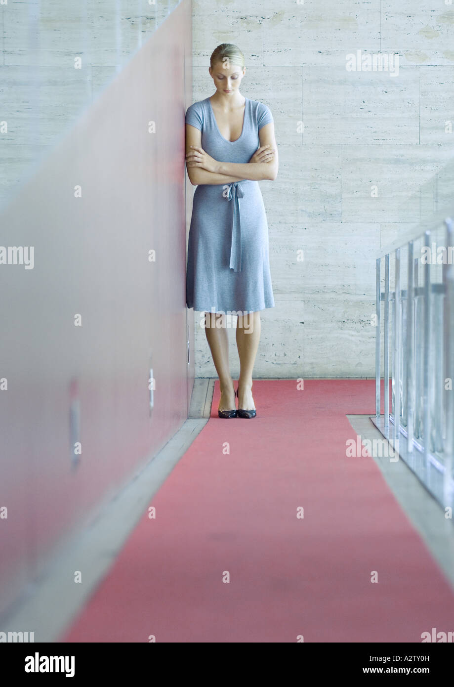 Woman standing, leaning against wall, head down, full length portrait ...