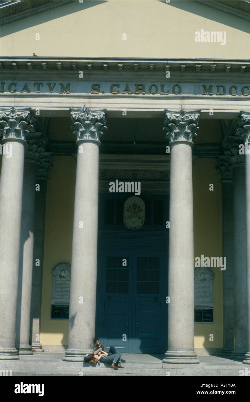 young couple hugging and sitting below tall pillared building, milan ...