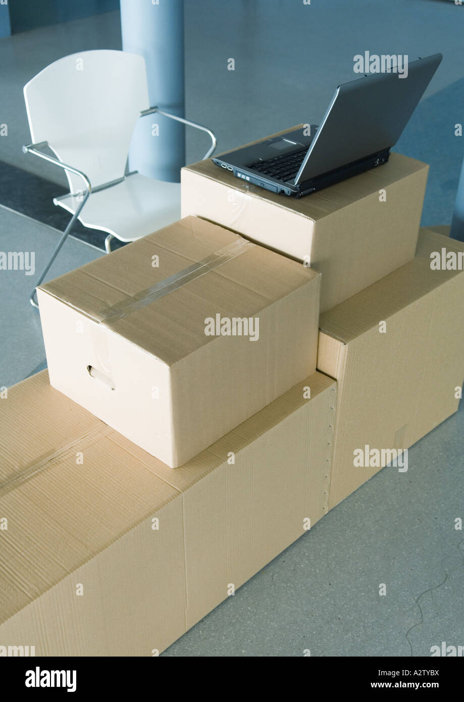 Open laptop on stack of cardboard boxes, and empty chair Stock Photo ...