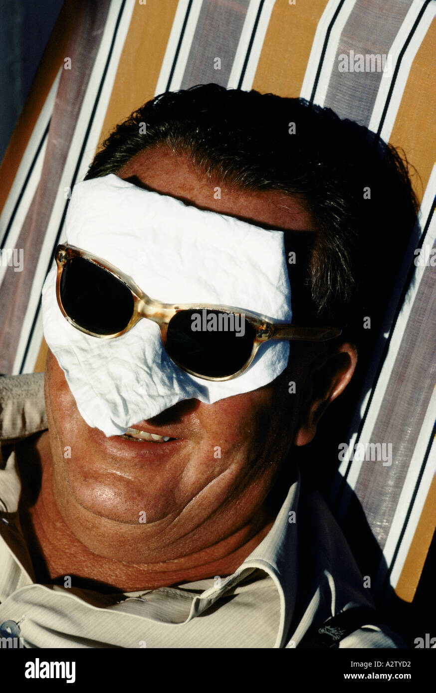 man sunbathing with his face covered with handkerchief sunglasses on ...