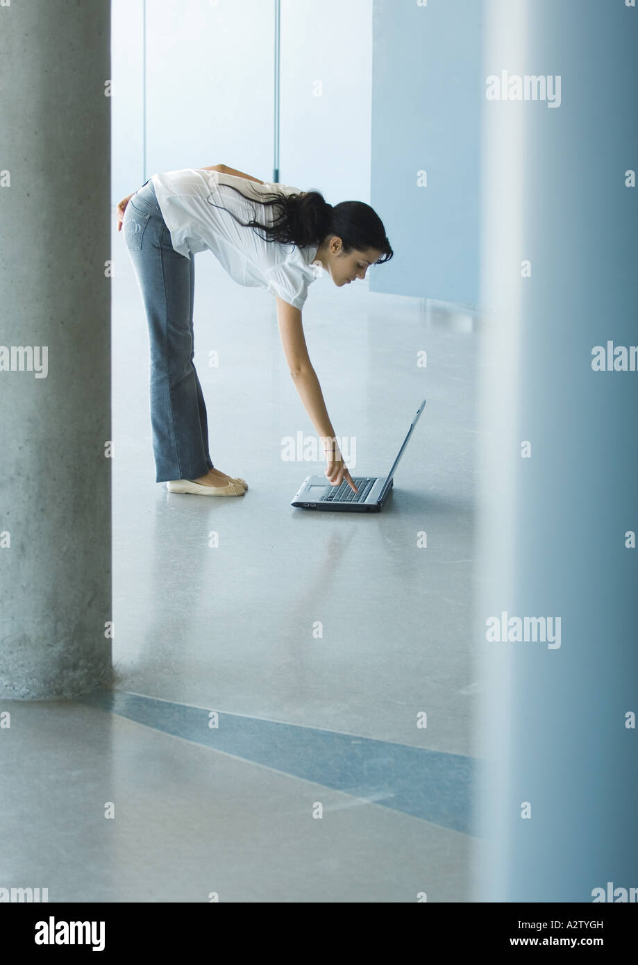 Young woman bending over, pressing key on laptop Stock Photo - Alamy