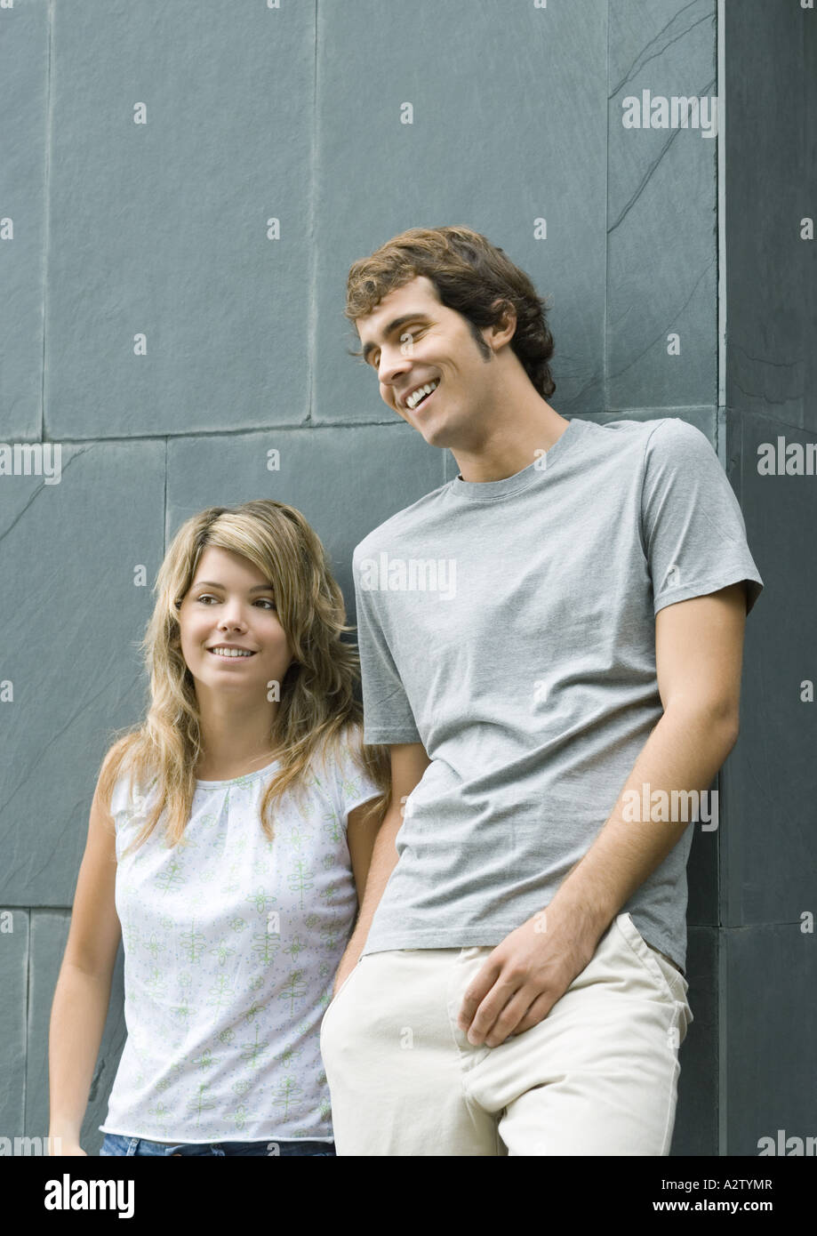Young man and woman leaning against wall, smiling Stock Photo - Alamy
