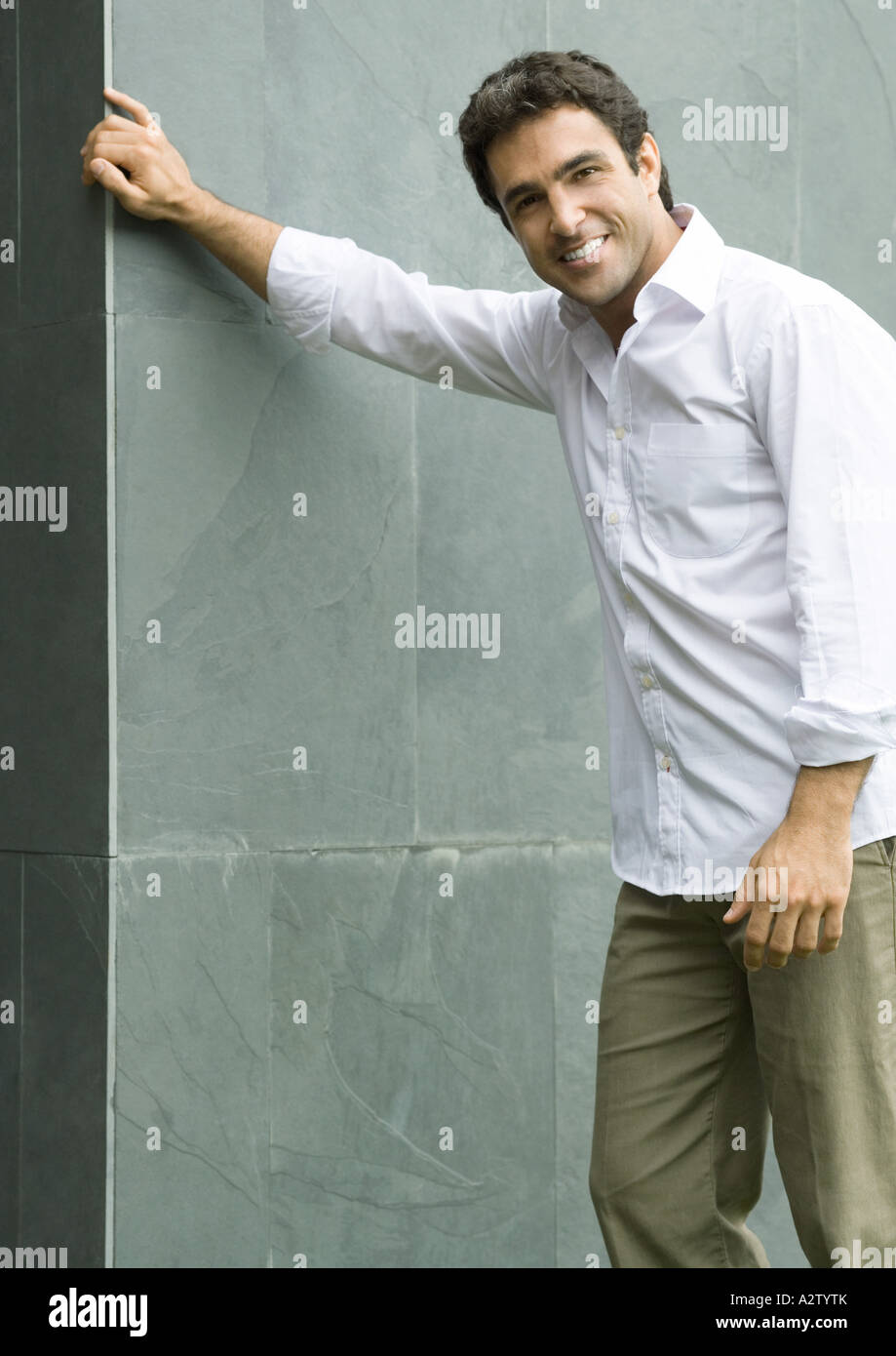 Man standing with hand on wall, smiling at camera, portrait Stock Photo ...