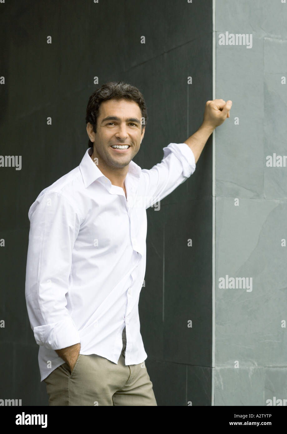Man standing with hand on corner of wall, smiling at camera, portrait ...