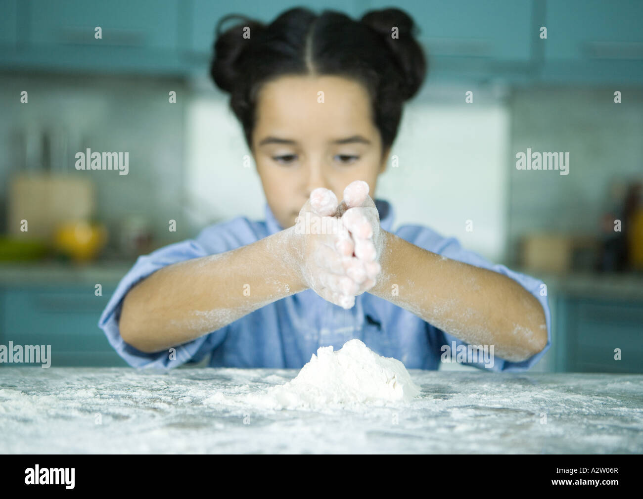 Girl standing at kitchen counter, holding hands over pile of flour ...
