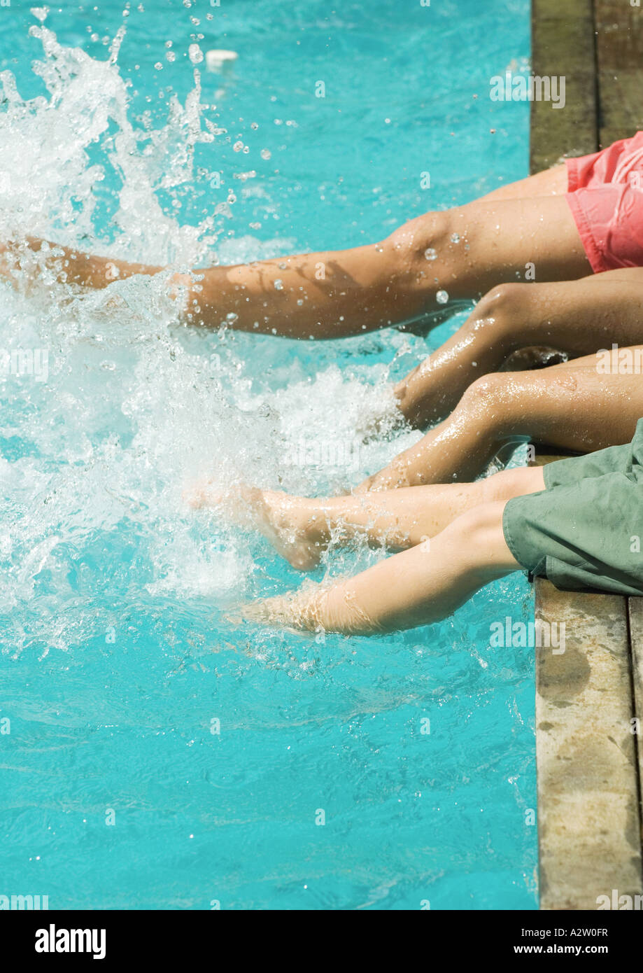 Man and children sitting on edge of swimming pool, splashing with legs ...
