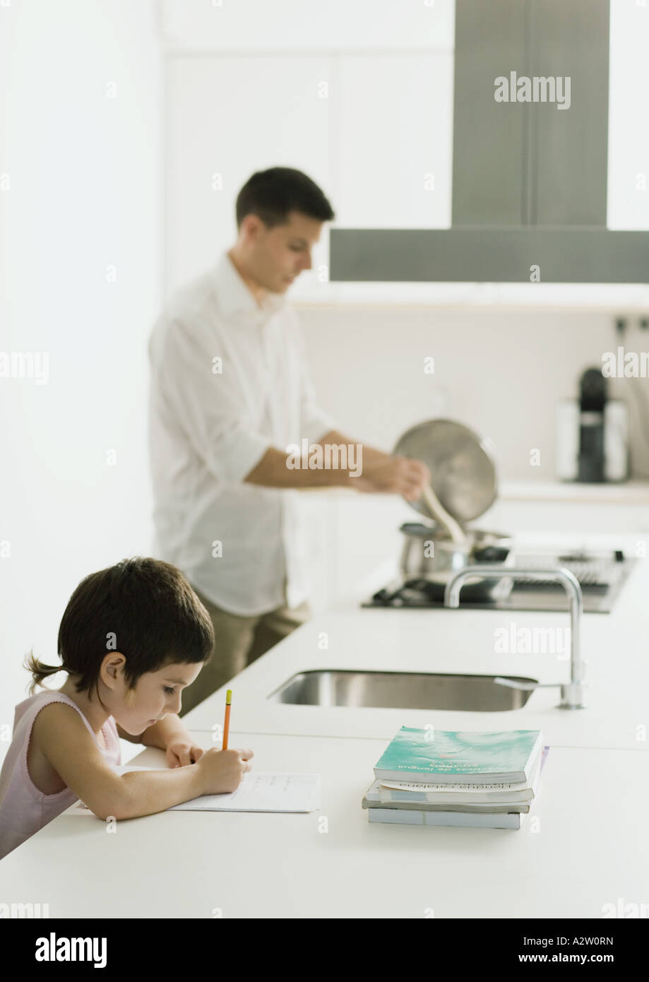 Child doing homework on kitchen counter while father cooks Stock Photo ...