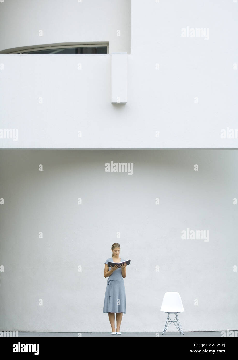 Woman standing next to chair, reading book Stock Photo - Alamy