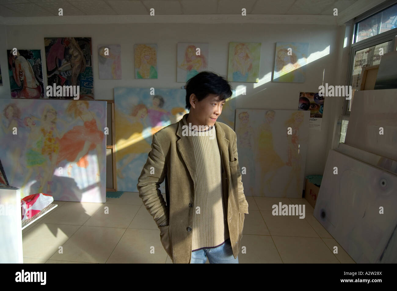Portrait of a young Chinese artist in front of some of his paintings ...