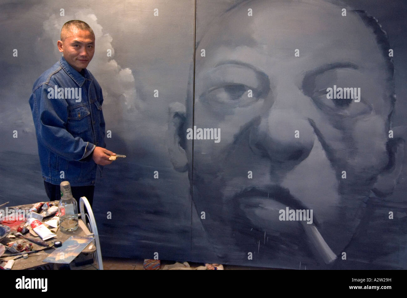 Portrait of a Chinese artist painting on a large canvas in the small ...