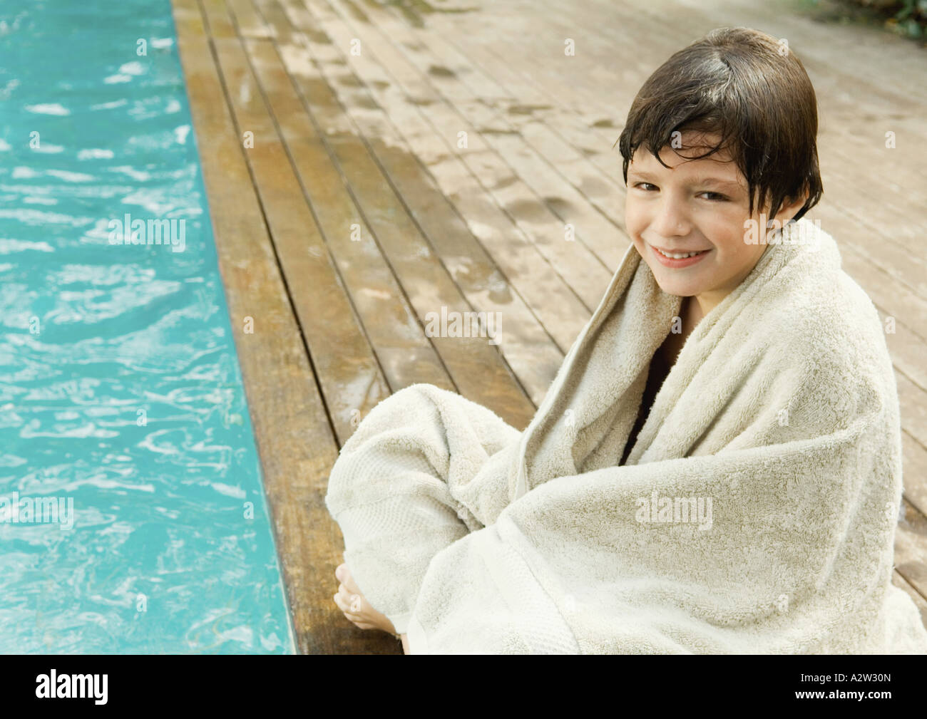 Little boy sitting by edge of swimming pool, wrapped in towel Stock ...