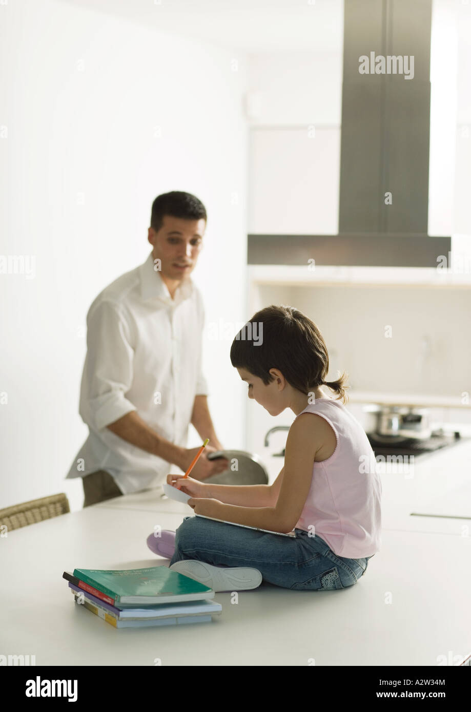 Child sitting on counter doing homework while father cooks meal Stock ...