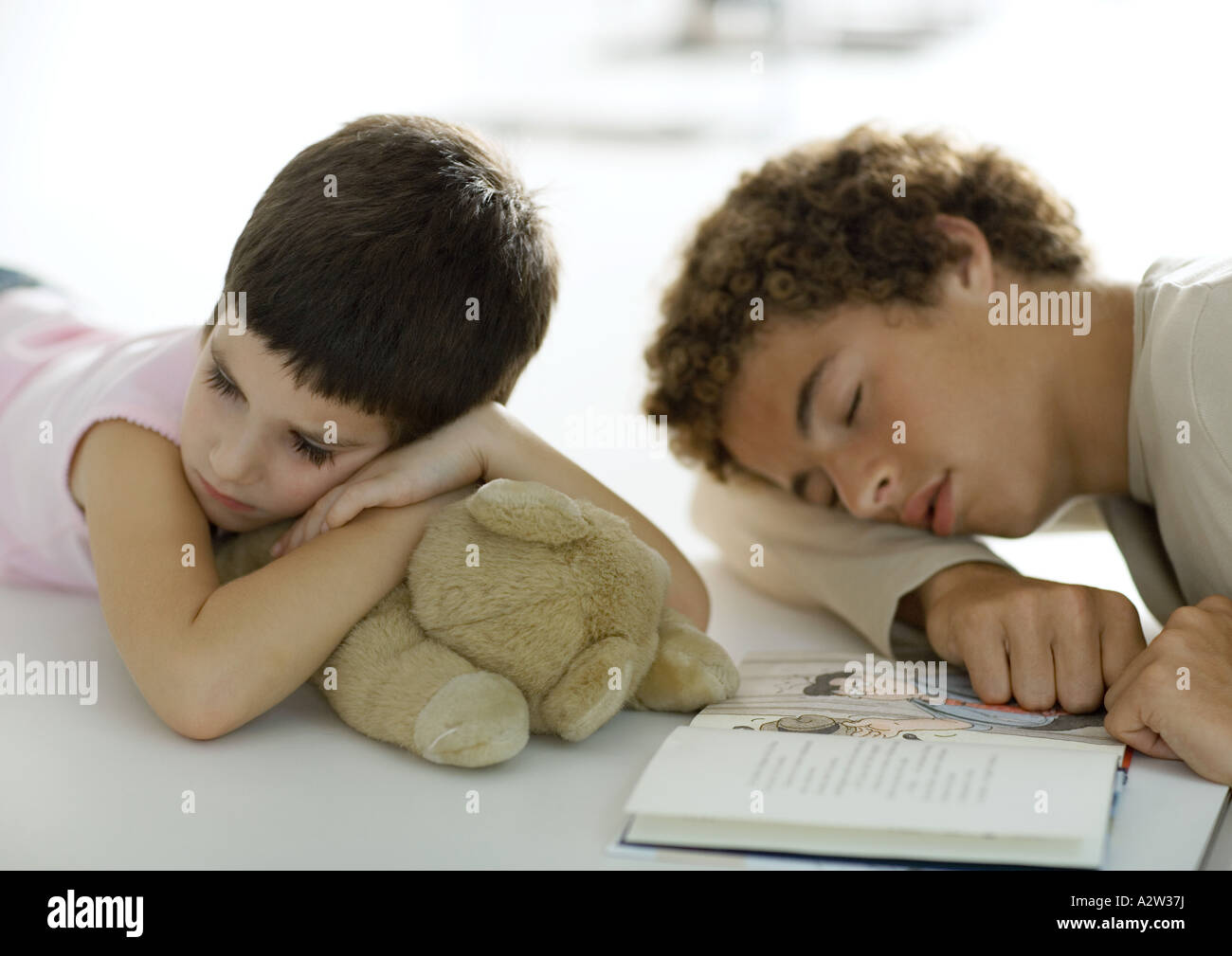 Adolescent boy and younger sibling falling asleep while reading book ...