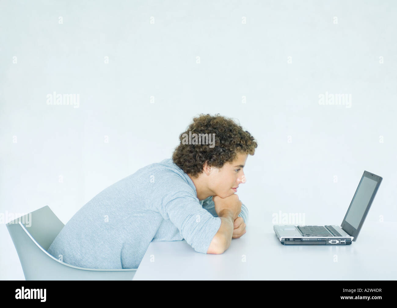 Young man sitting, leaning on desk, facing laptop computer Stock Photo ...