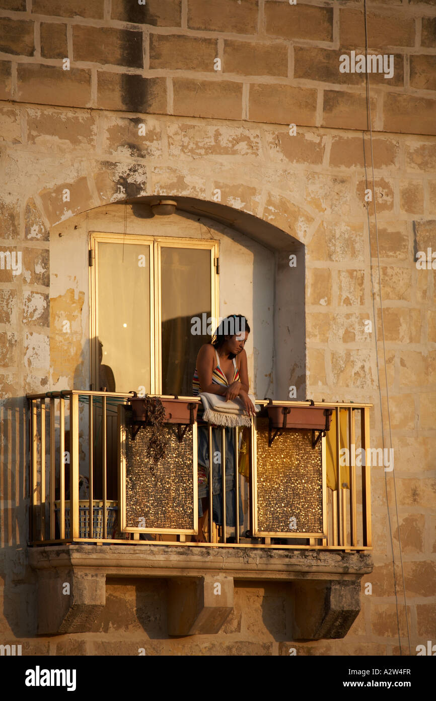 Woman looking out from balcony in evening sunlight in Valetta capital ...