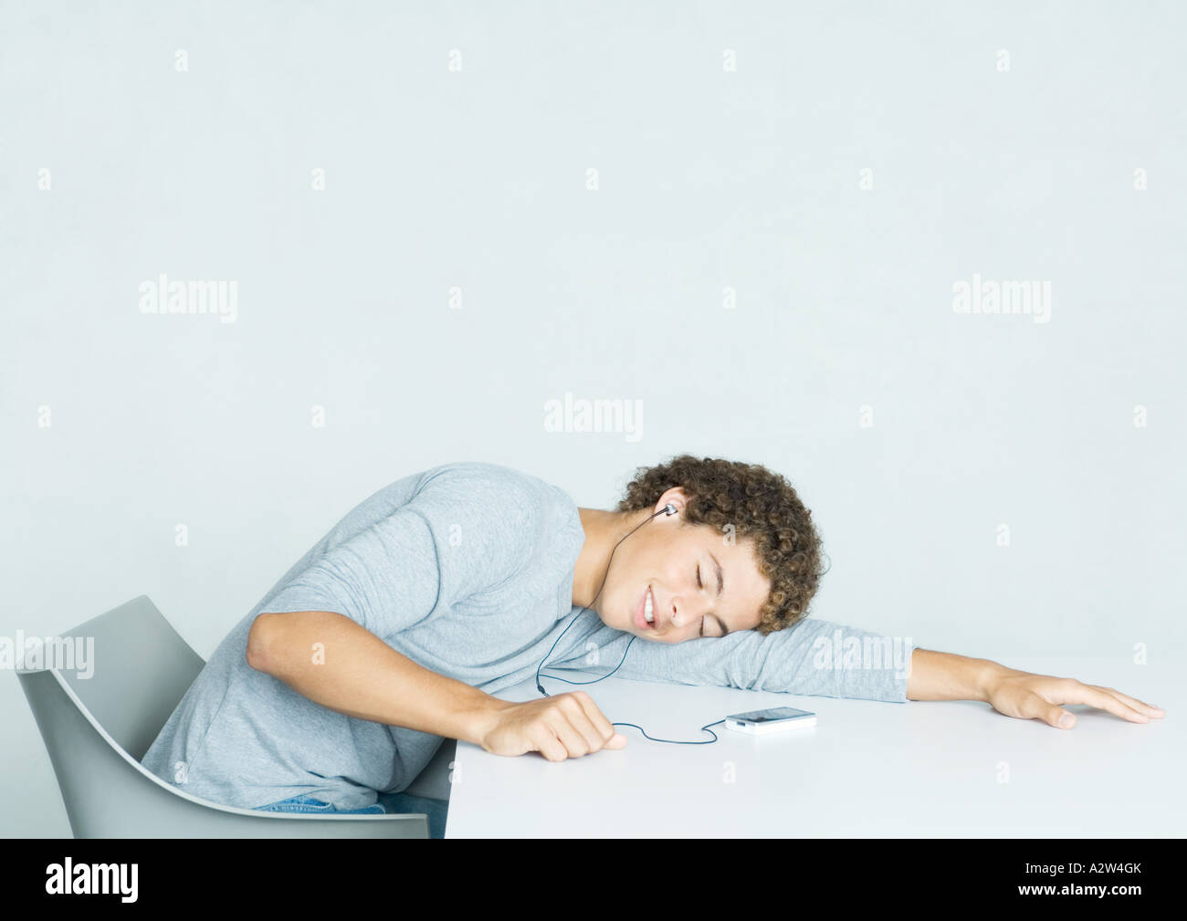 Young man sitting with head on table, listening to portable MP3 player ...