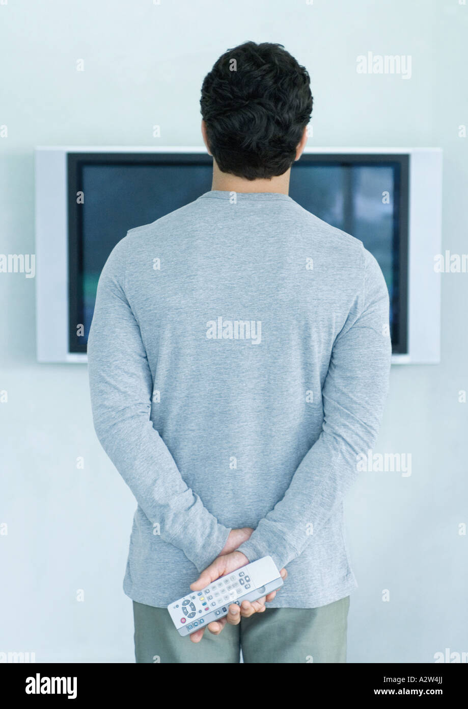 Man standing in front of widescreen TV, holding two remote controls ...