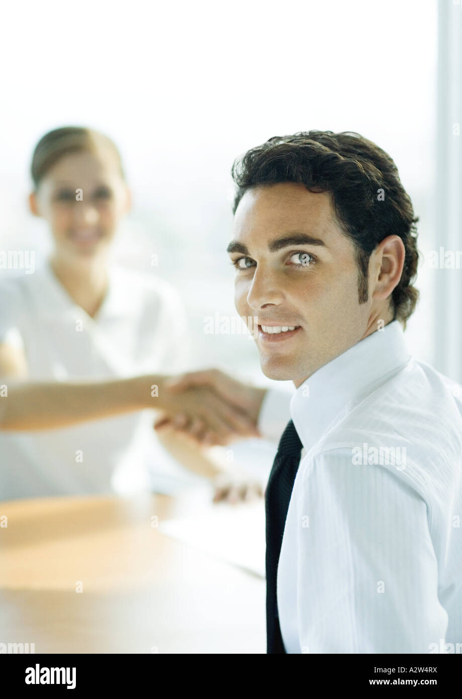 Man and woman shaking hands across table, man smiling over shoulder at ...