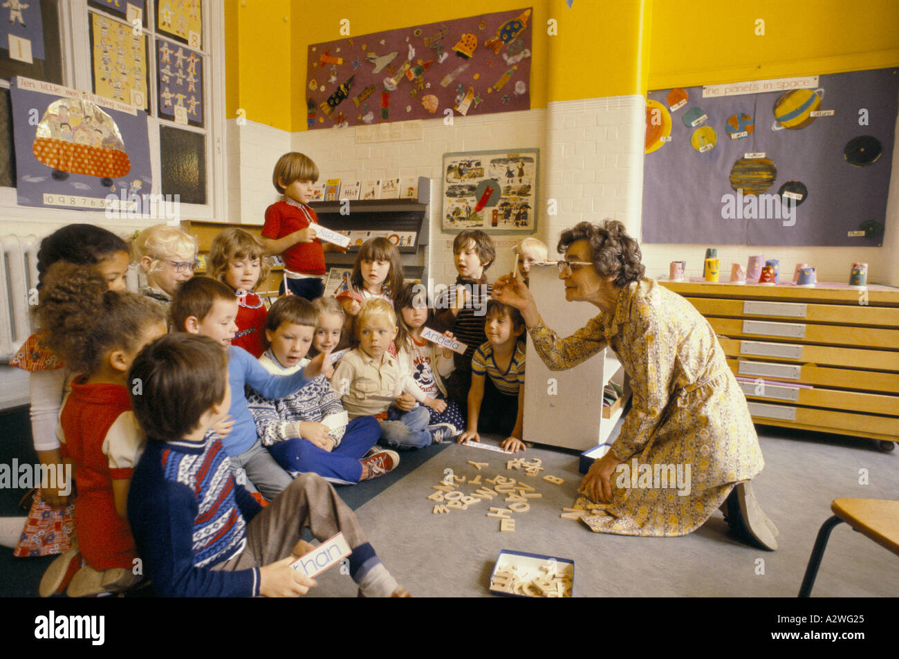 junior school teacher showing letters of the alphabet to group of young ...