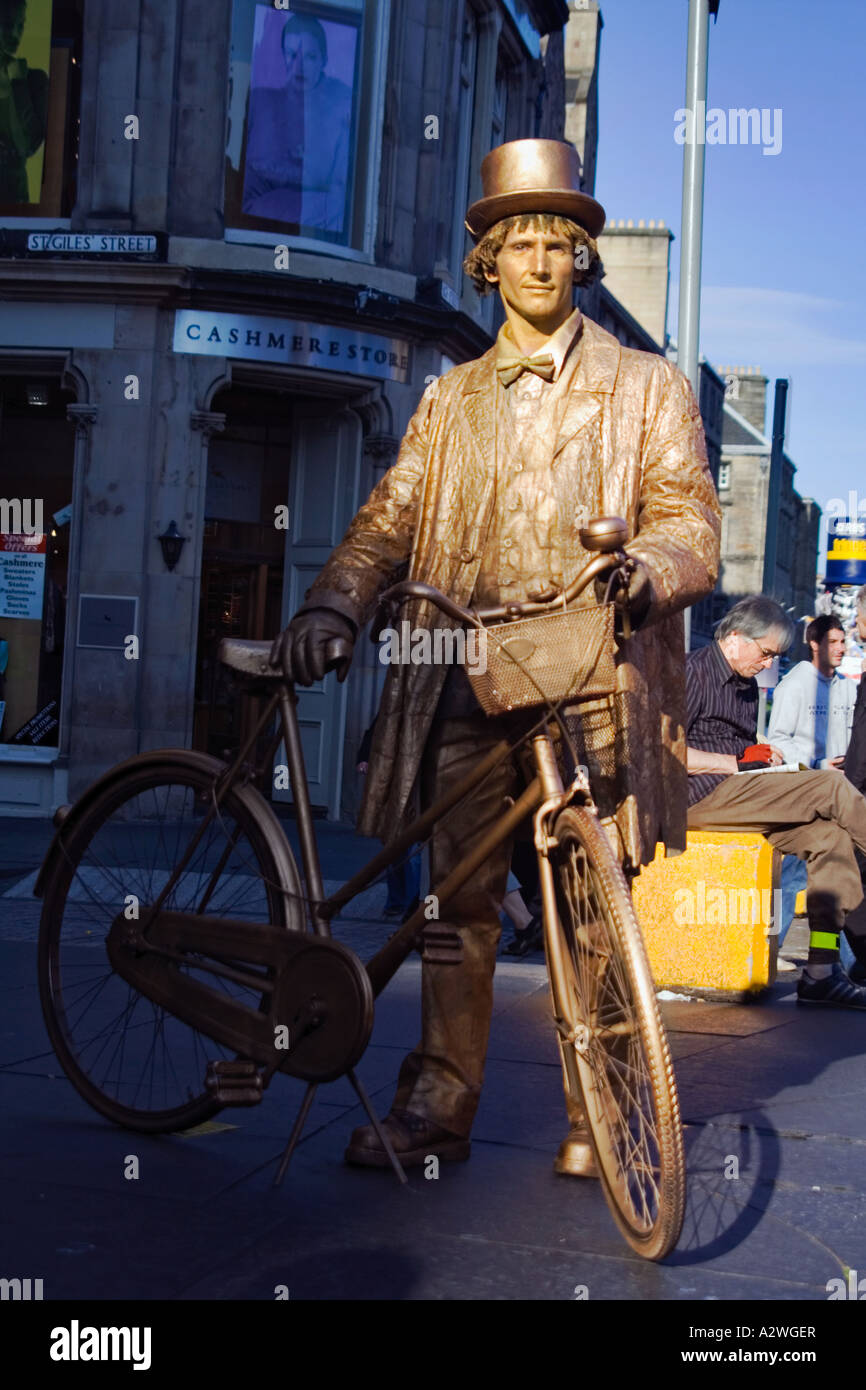 Mime artist dressed as a golden living statue with a bicycle entertains ...