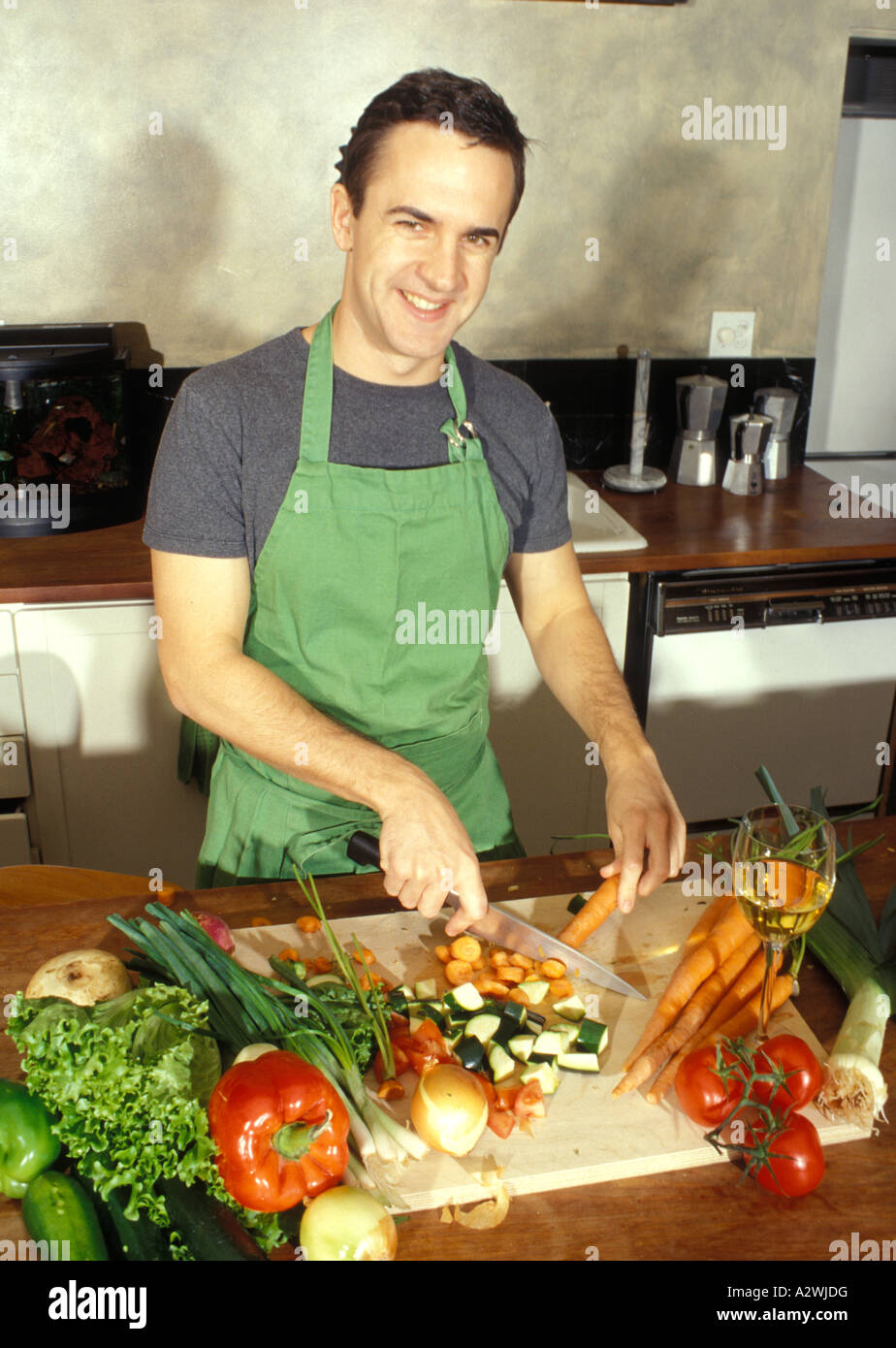 Young man cutting vegetables in kitchen, smiling, portrait Stock Photo ...