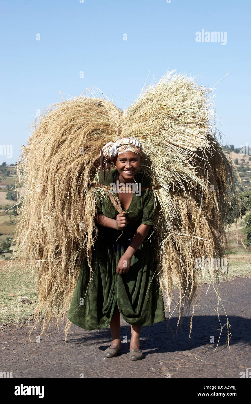 Woman smiling walking working on a road carrying heavy load of crops ...