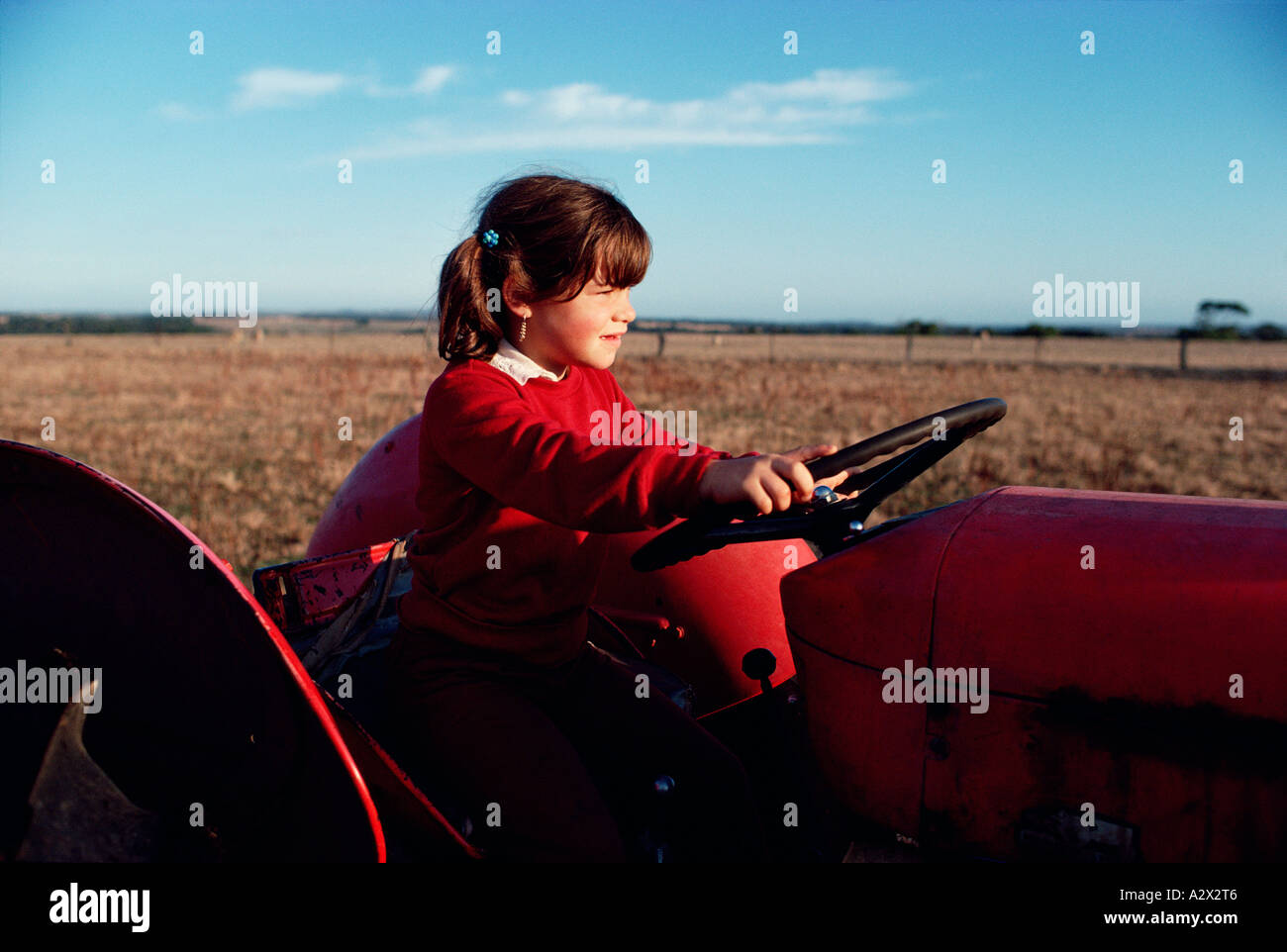 Outdoor close-up of little girl child playing on farm tractor ...