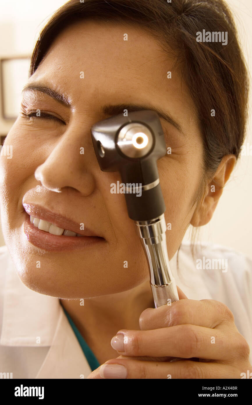Female physician holds an otoscope to her eye during an examination of ...