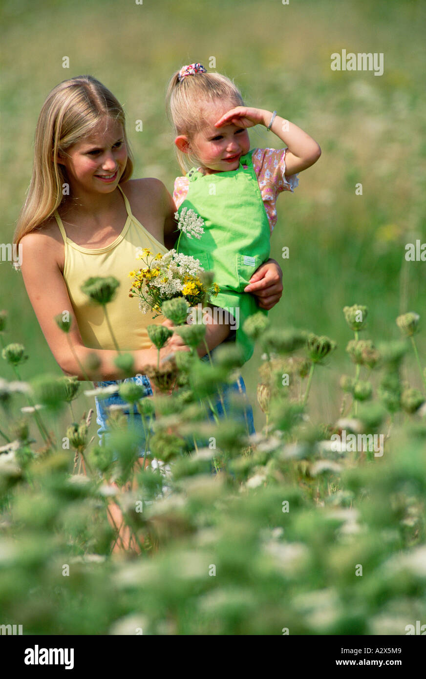 Close-up of young blond woman carrying little girl child outdoors in ...