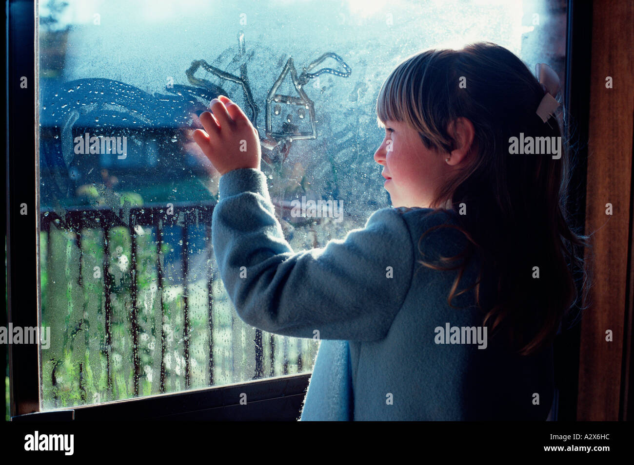 Children. Little girl Indoors drawing with fingers on damp window pane ...