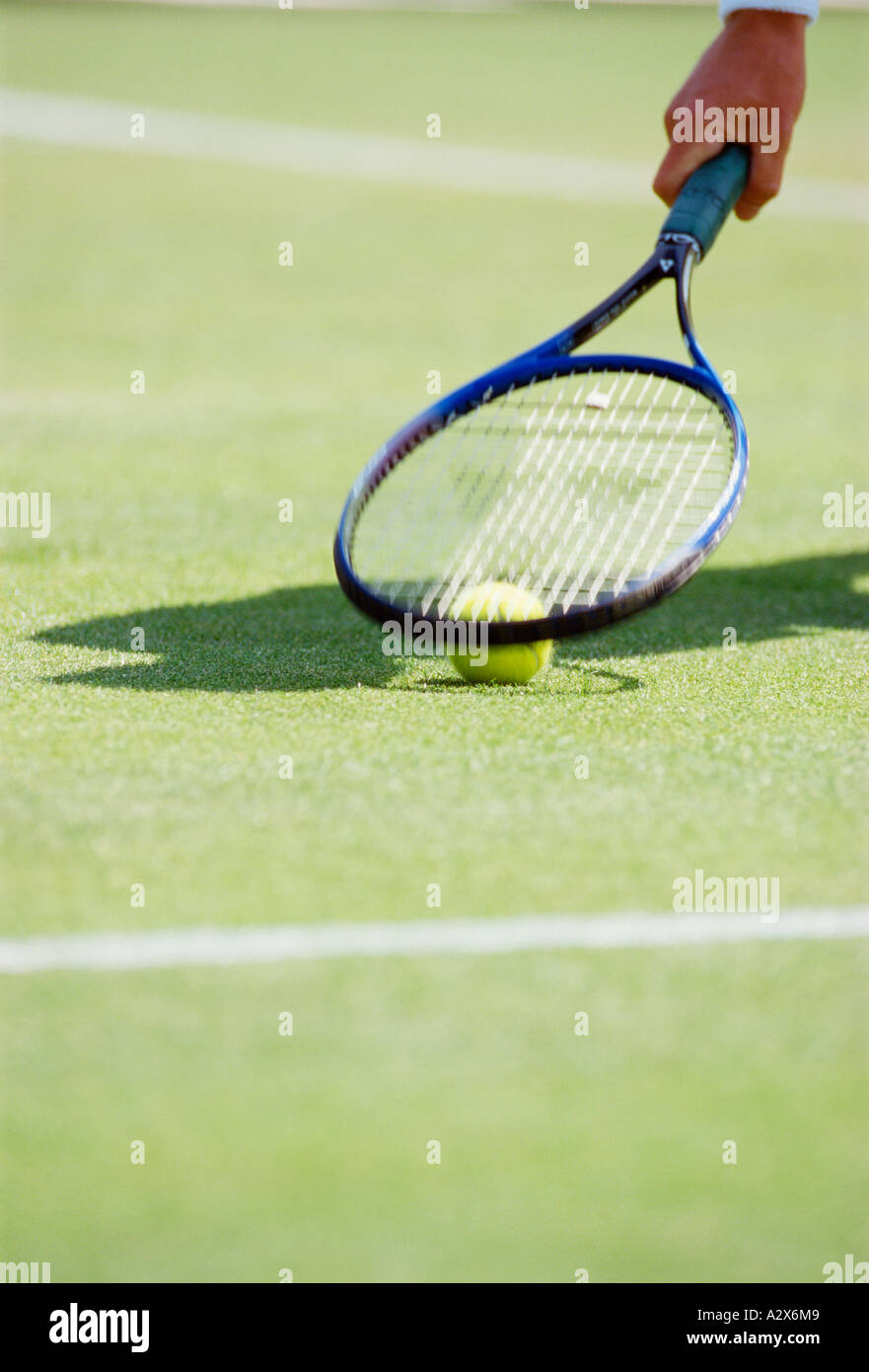 Outdoor close-up of man's hand with tennis racket and ball on grass ...