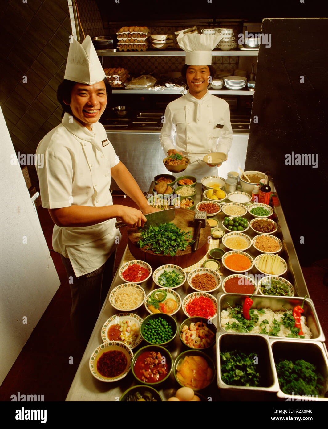 Two Asian male chefs in hotel restaurant kitchen preparing food ...