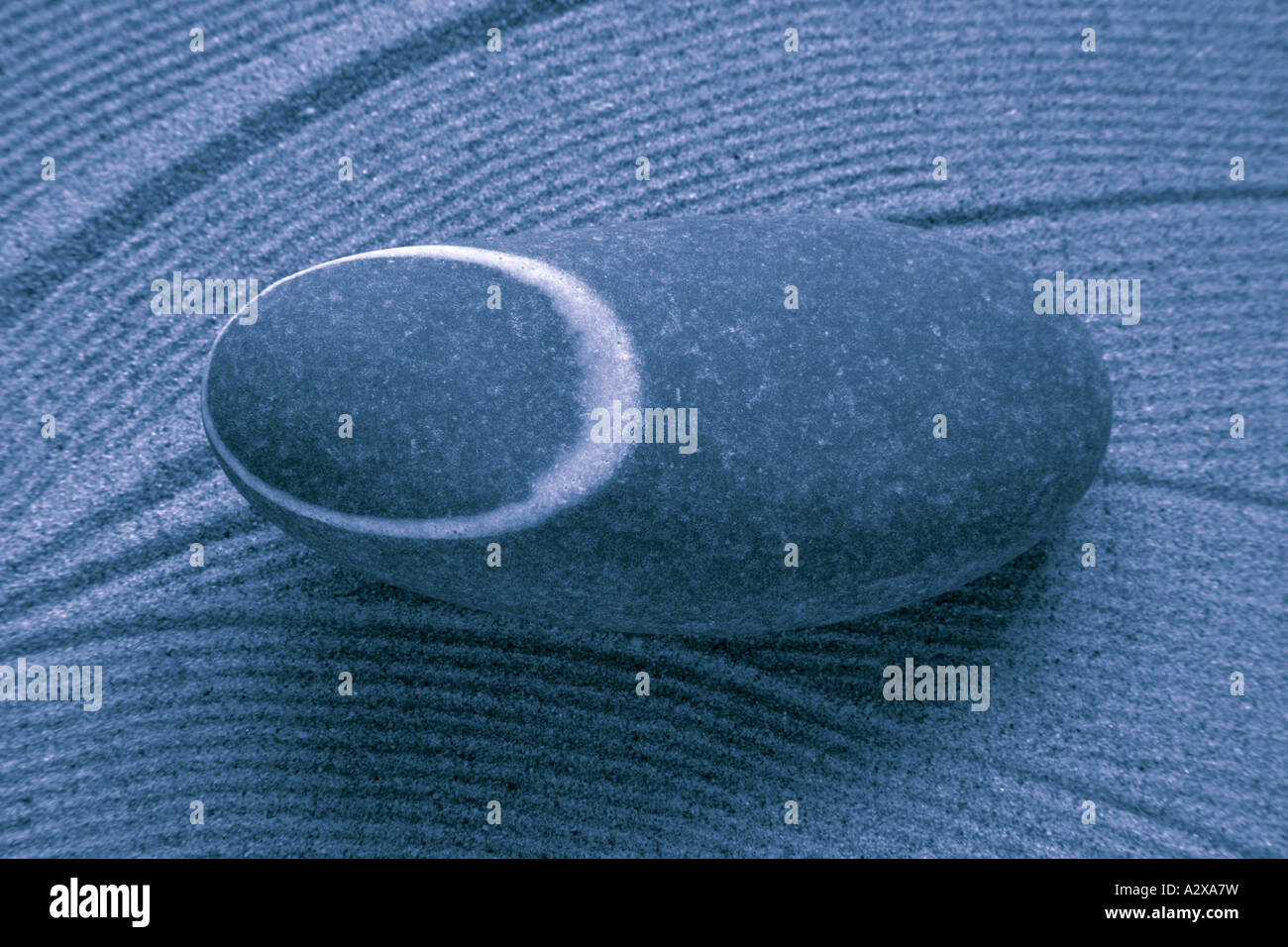 Zen stone on raked sand in blue Stock Photo - Alamy