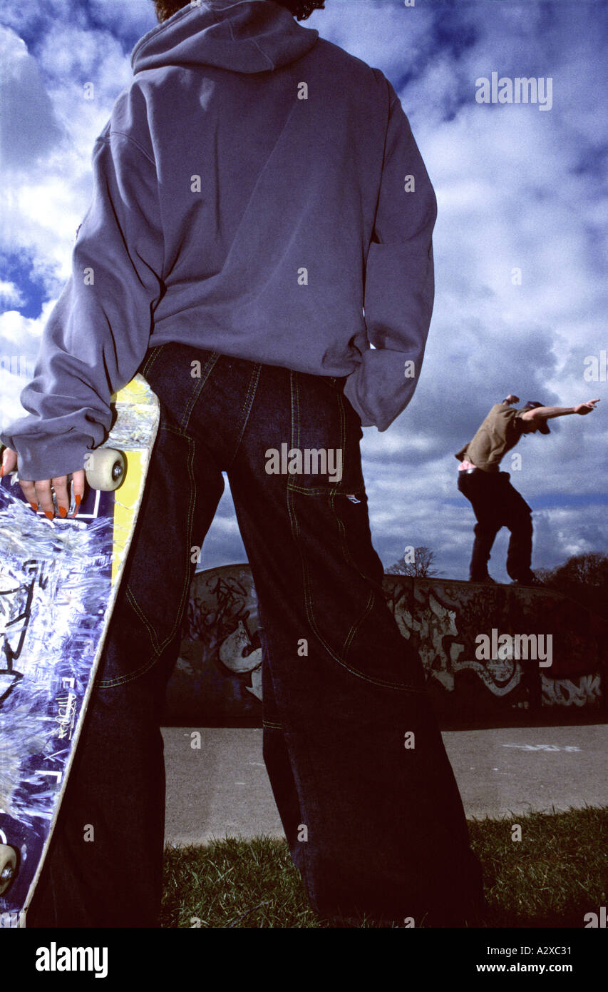 Back view of girl with skateboard with another skateboarder behind ...