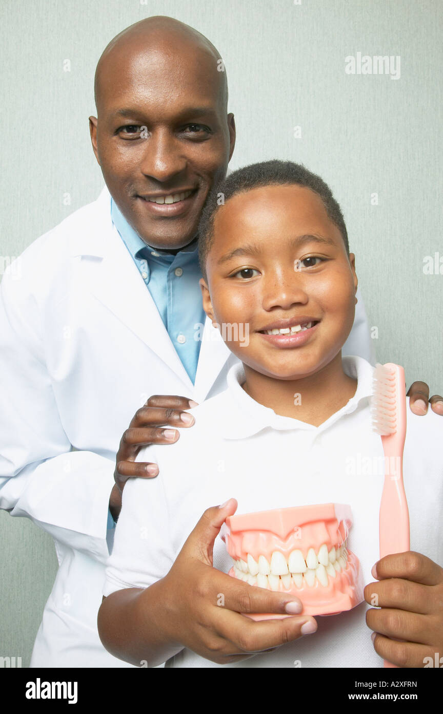 African male dentist with boys holding toothbrush and model of teeth ...
