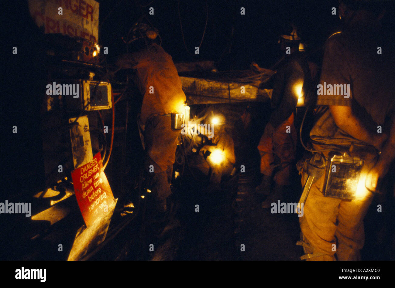 COALMINERS AT WORK IN DARKNESS UNDERGROUND. IN ORANGE OVERALLS ...