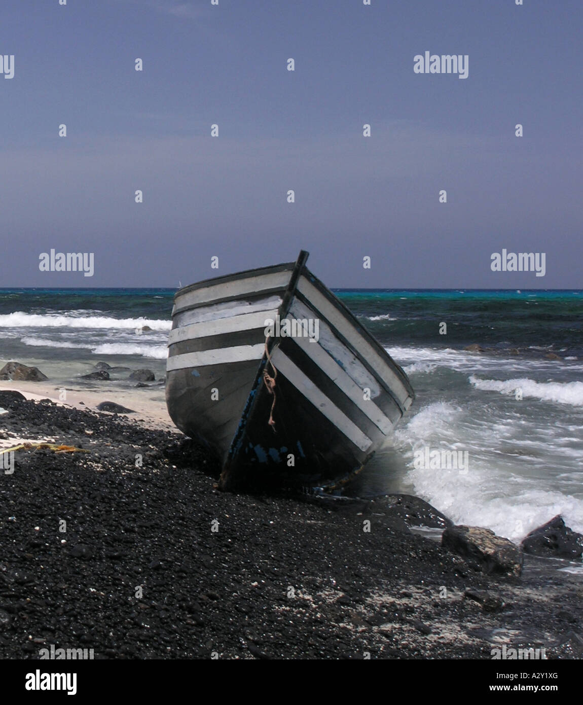 Fishing boat on the shore line of a volcanic grit beach in Lanzarote ...