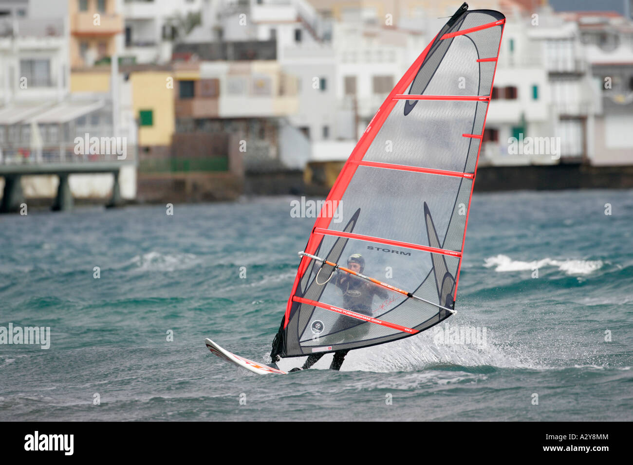 male windsurfer in wetsuit and red lined kite goes the waves in front ...