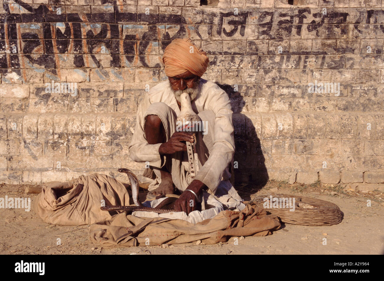 Snake charmer playing pipes and crouching against a wall India Stock ...