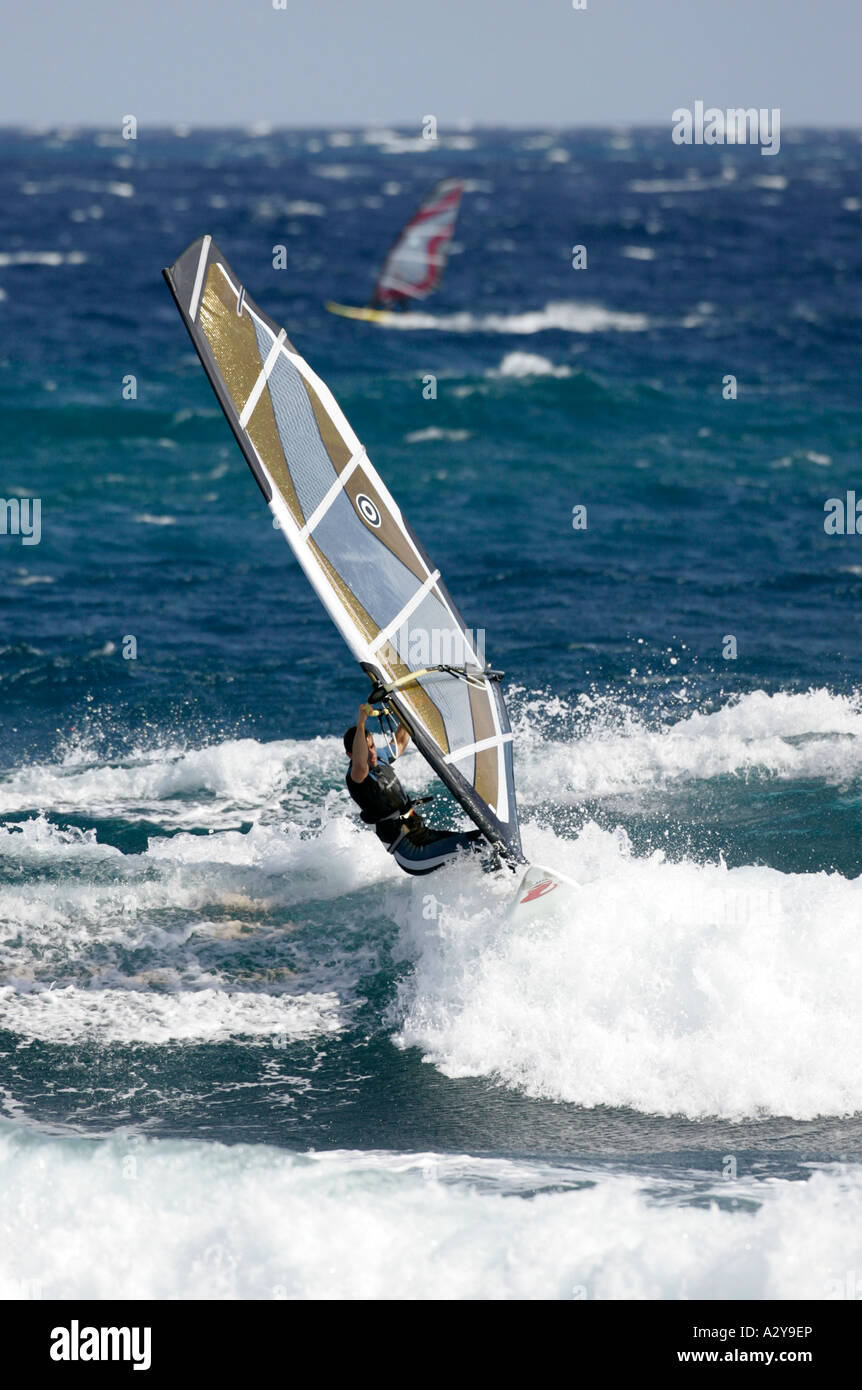 male windsurfer in wetsuit rides his board along the crest of a wave ...