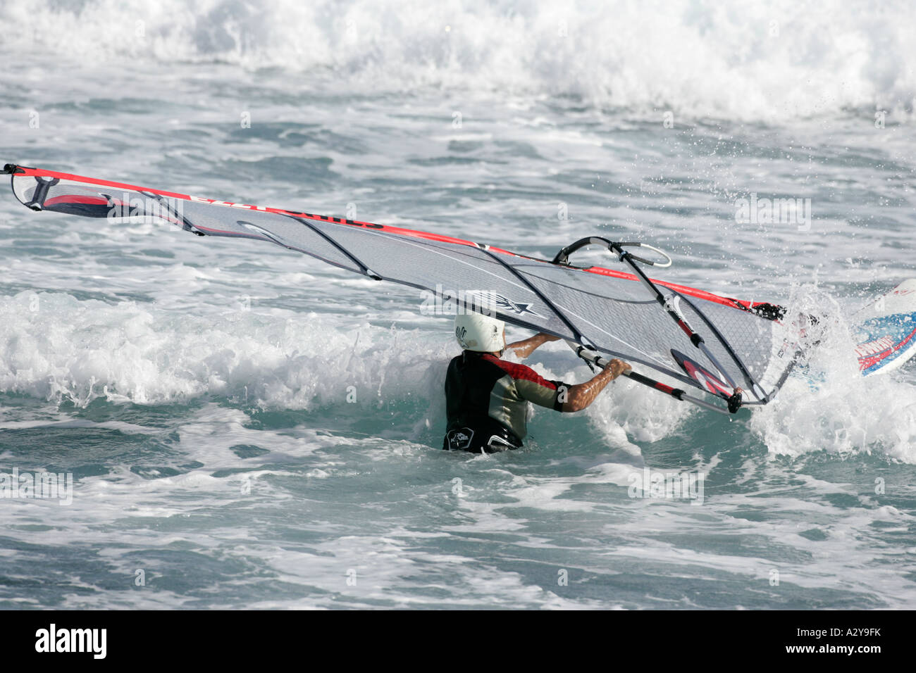 male windsurfer in wetsuit and helmet pushes his board through foamy ...