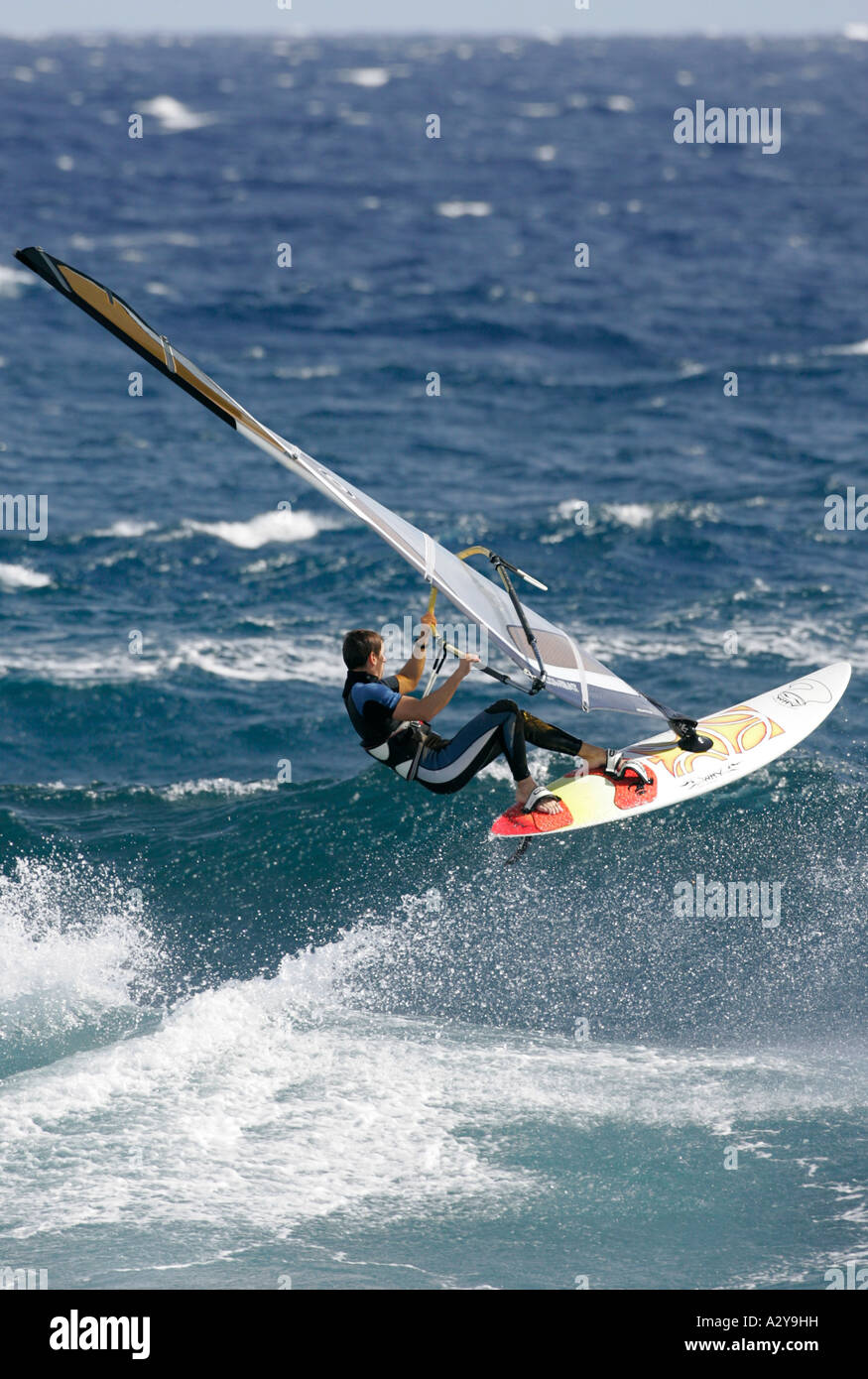 male windsurfer in wetsuit launches their board at speed into the air ...