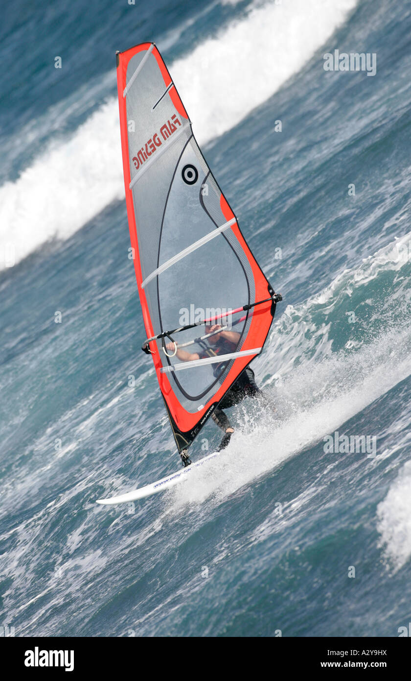 windsurfer in wetsuit rides their board at speed through the waves in ...