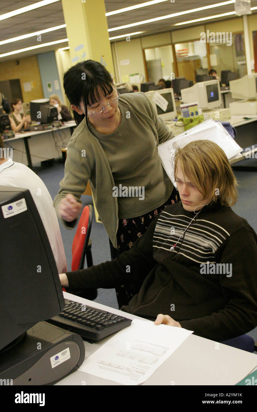 Teenage male student with computer and instructor in sixth form college ...
